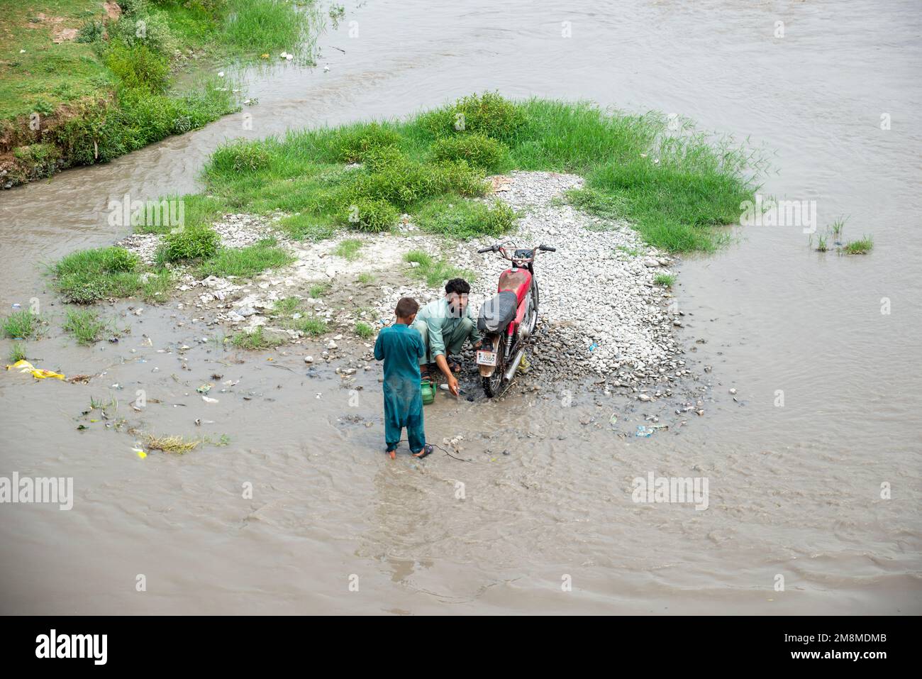Two adult men washing motorcycle on the Bara River, Peshawar, Pakistan ...