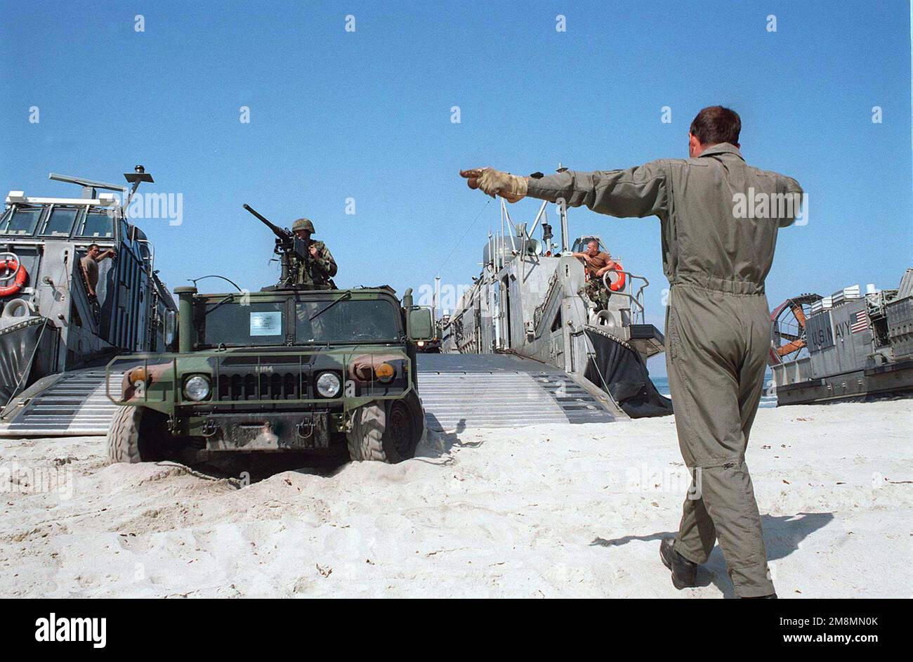 A US Navy loadmaster directs a HMMWV, mounted with a machine gun, from ...