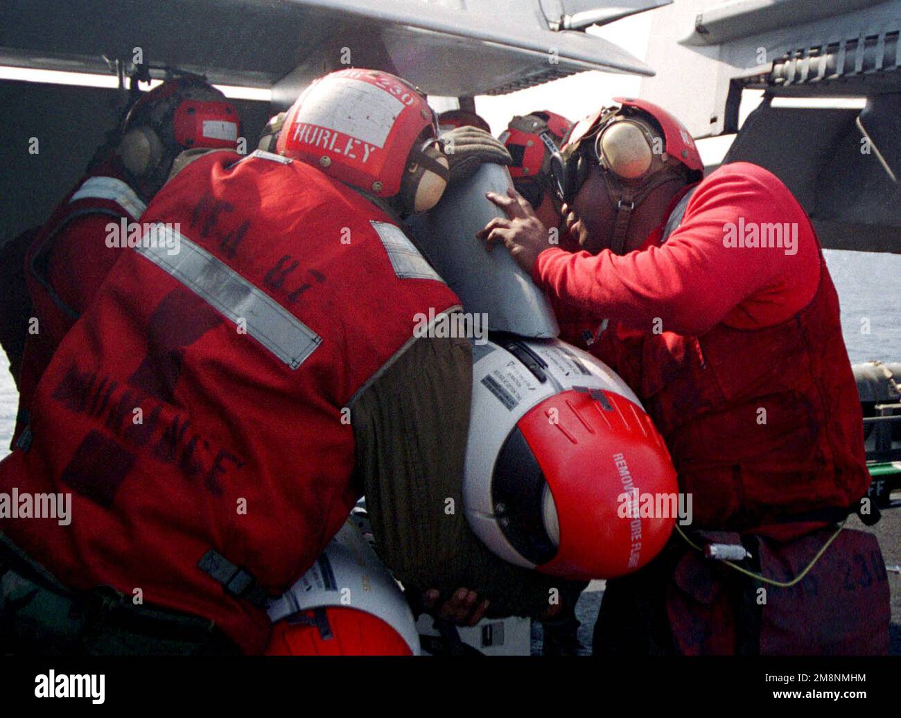 Aviation Ordnancemen load Rockeye cluster bombs on to the wing of an F ...