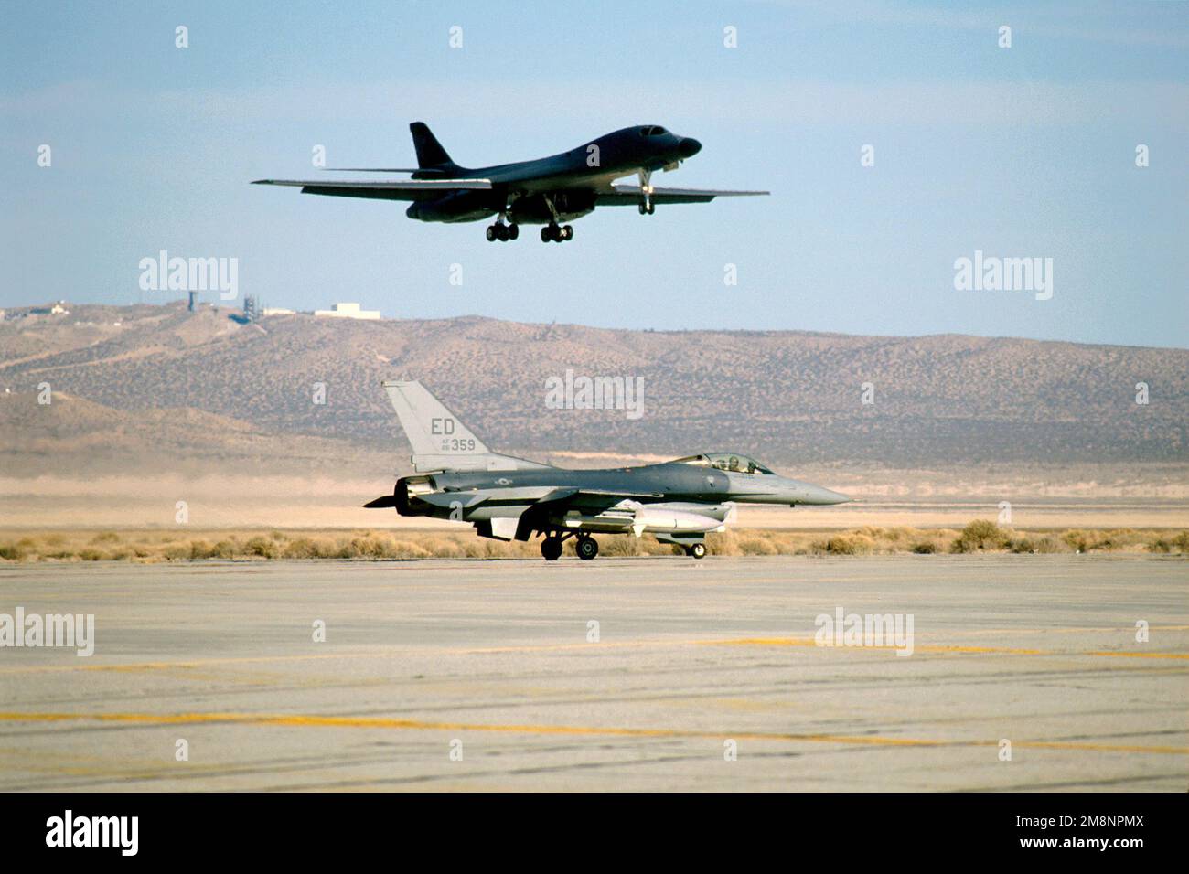 An F-16 Fighting Falcon waits as a B-1 Lancer lands after a flight test ...