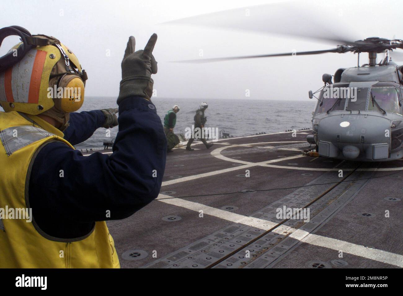 US Navy Boatswain's Mate 3rd Class Adrian Roble signals to the pilots ...