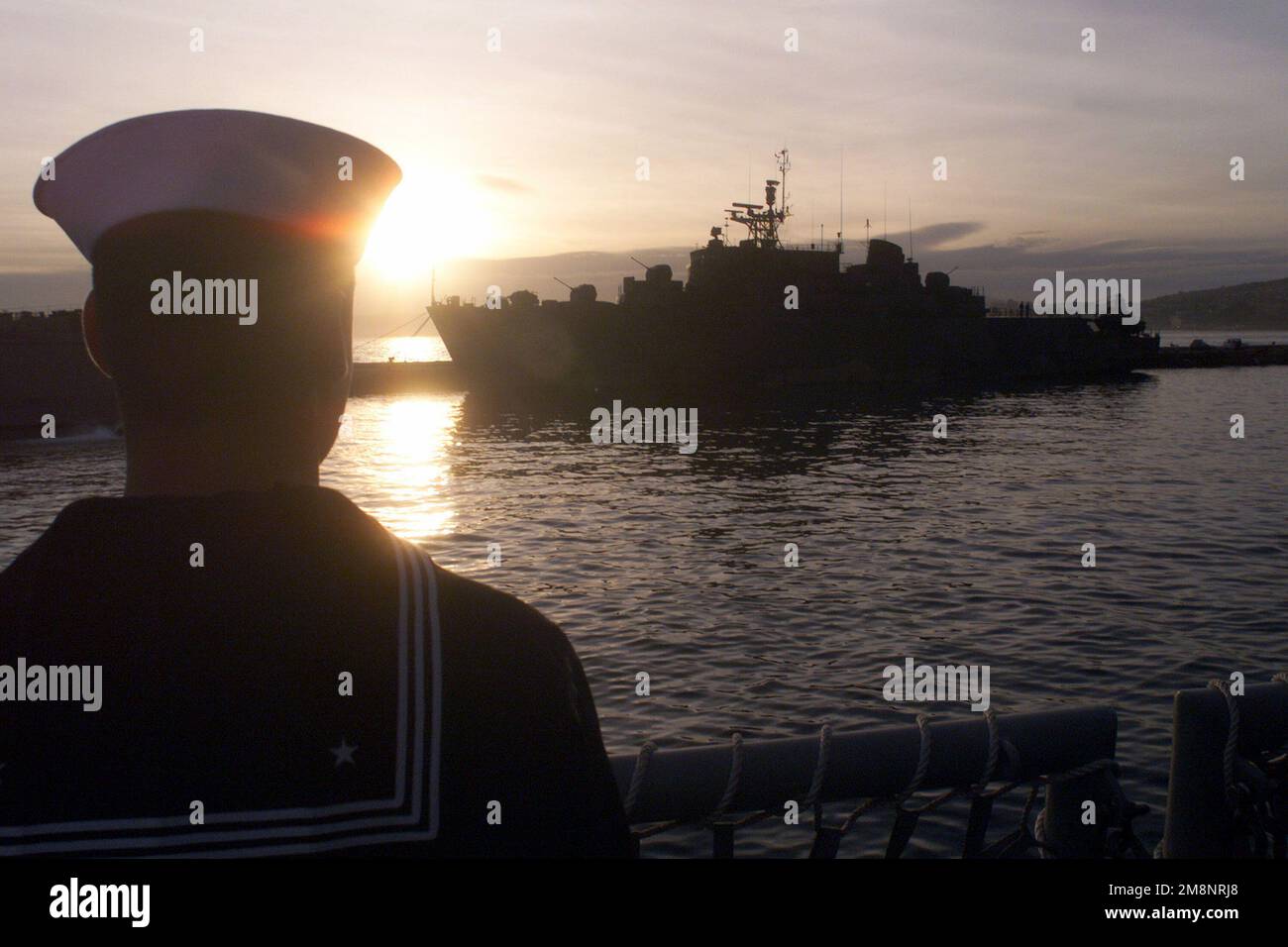 The early sun rises behind a Chilean naval vessel while a sailor aboard ...