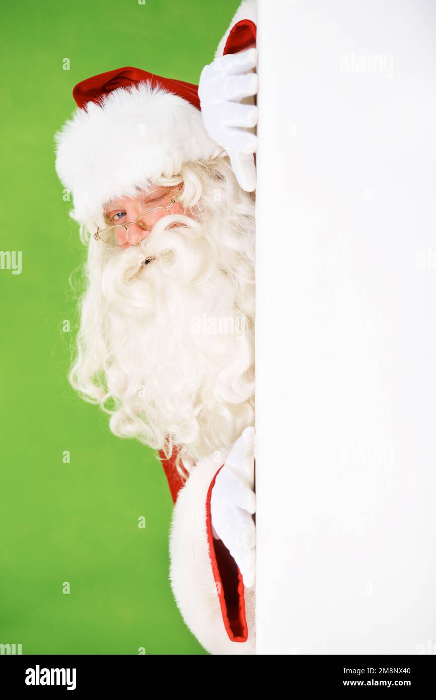 Our little secret. Father Christmas hiding behind a white wall, giving ...