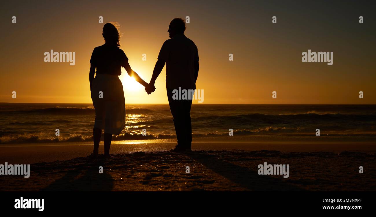 Silhouette of mature couple holding hands on the beach at sunset ...