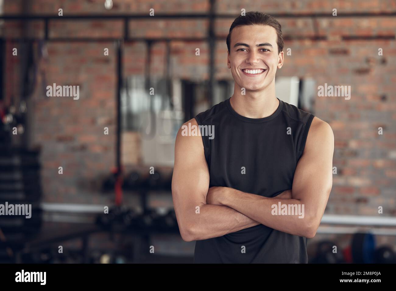 Portrait of a proud young man standing in the gym. Happy young man arms ...