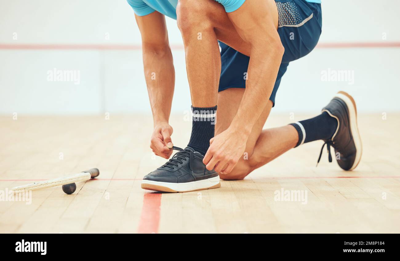 Unknown athletic squash player kneeling and tying shoelaces before ...
