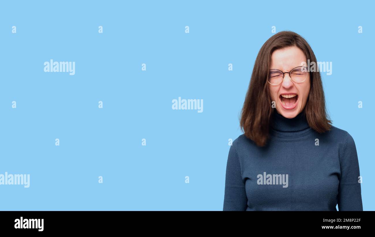 A stressed student girl in glasses and a sweater screaming on a blue ...