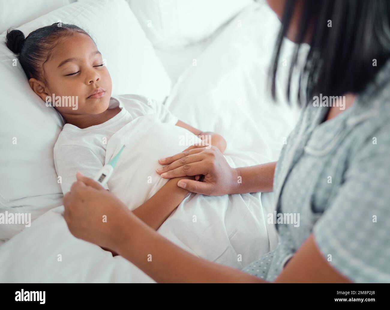 Sick little girl in bed while her mother uses a thermometer to check her temperature. Young ...