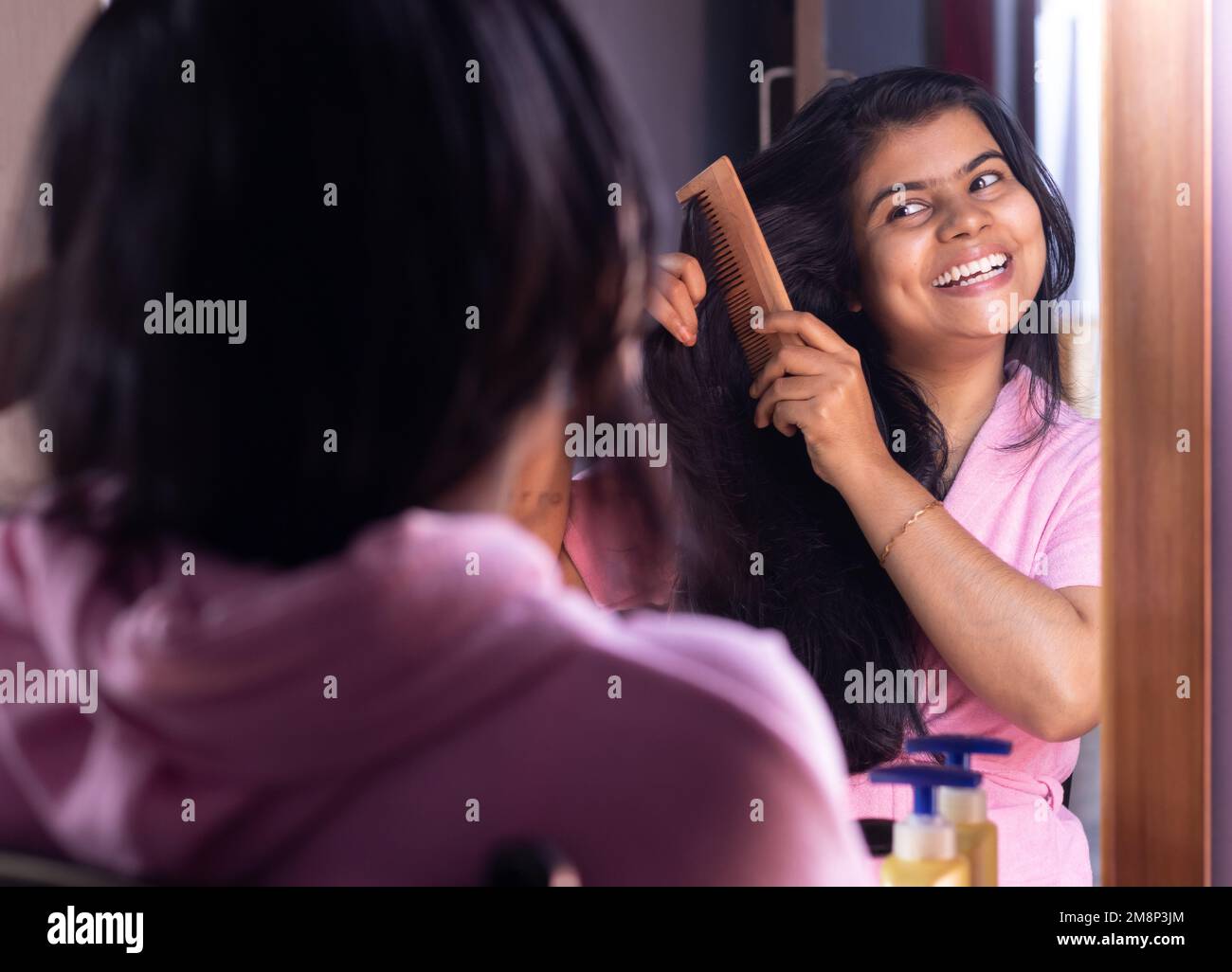 A pretty happy Indian woman brushing hair with wooden comb wearing ...