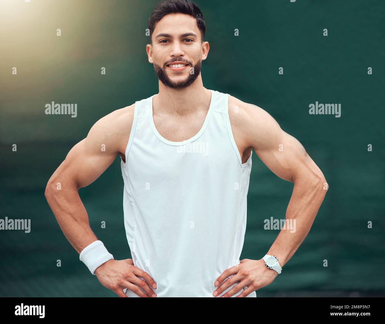 Portrait of smiling mixed race tennis player standing alone on a court ...