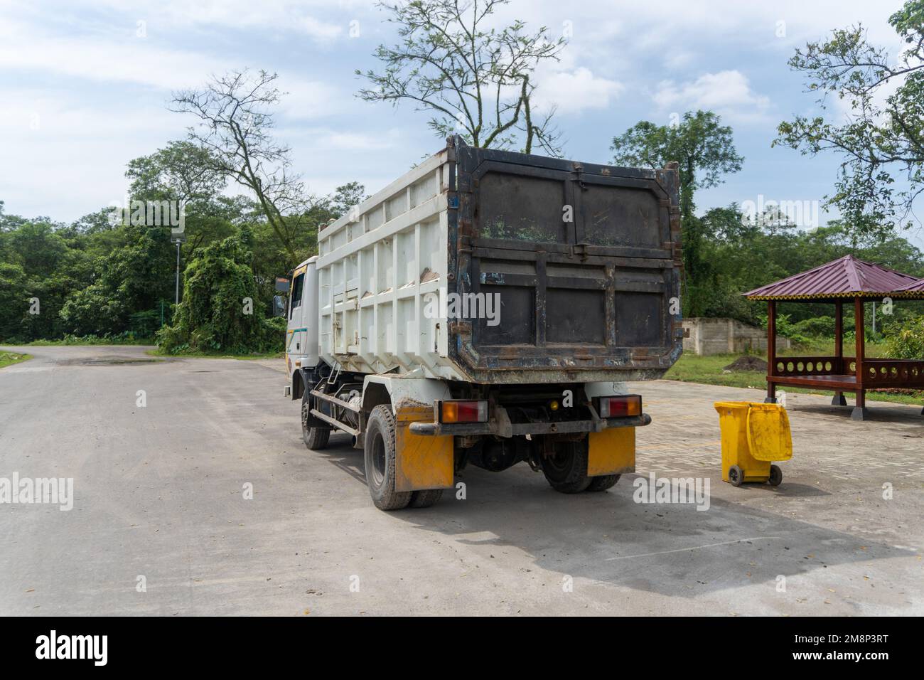 Logistics box truck is parked in city park near a yellow trash bin area ...