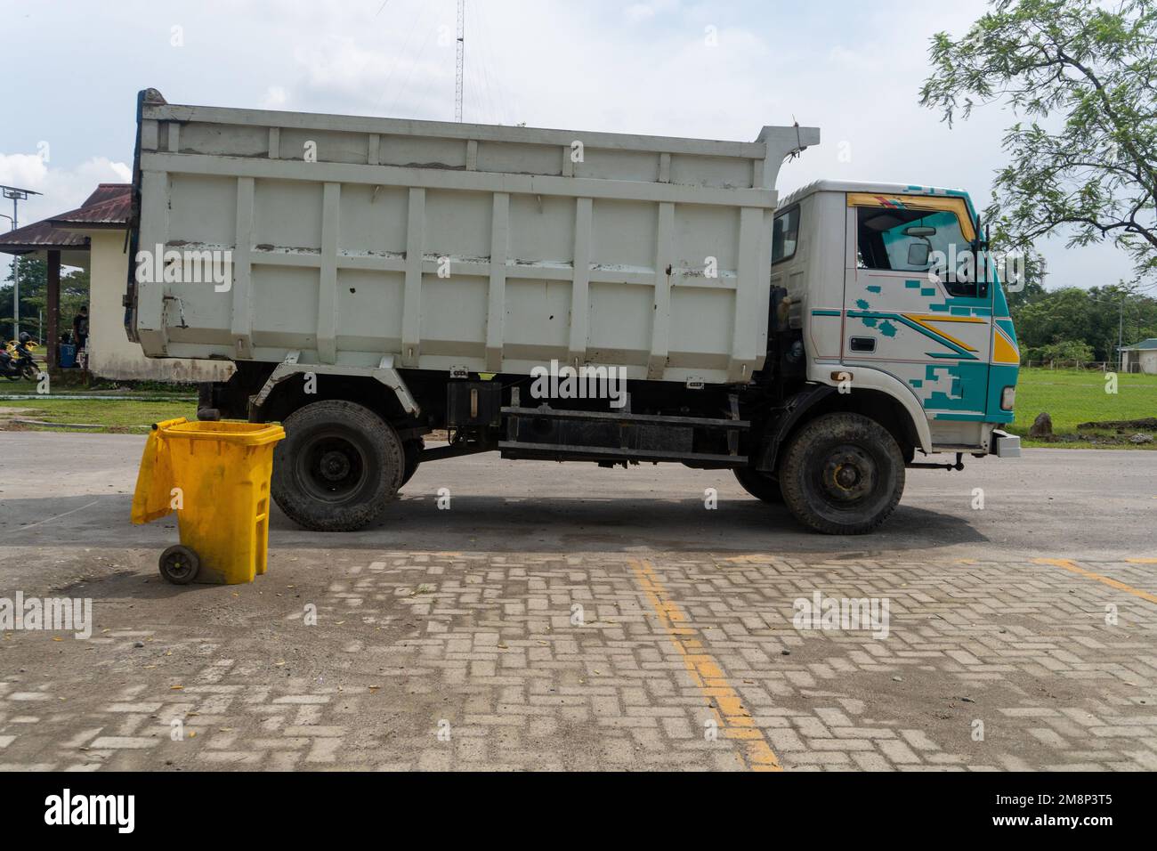 Logistics box truck is parked in city park near a yellow trash bin area ...