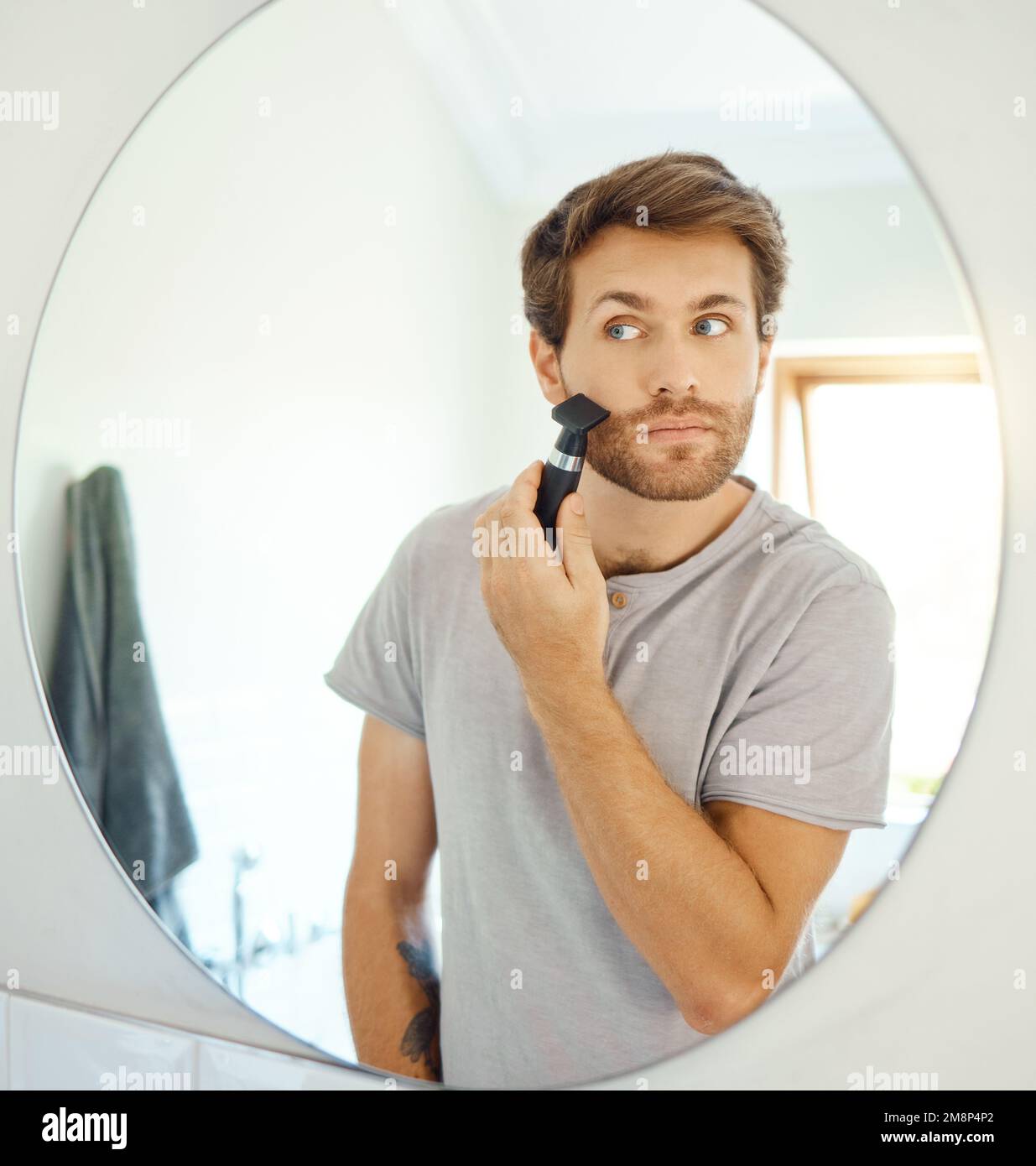 One handsome man shaving his face hair in a bathroom at home. Caucasian male using a shaver ...