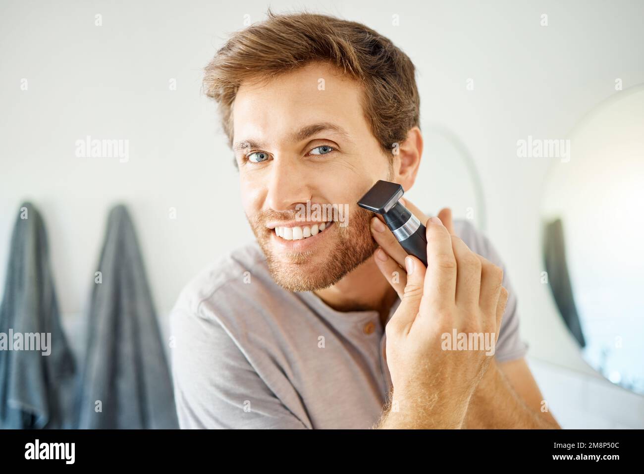One handsome man shaving his face hair in a bathroom at home. Caucasian male using a shaver ...