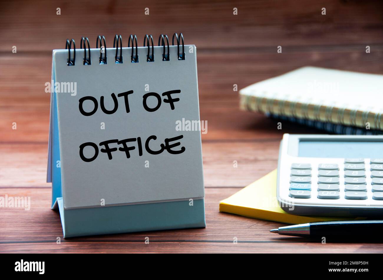 Out of office text on calendar desk with notebook, calculator and pen ...