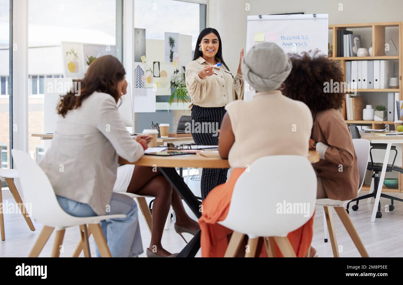 Ambitious indian business woman using a whiteboard for staff training in an office workshop ...