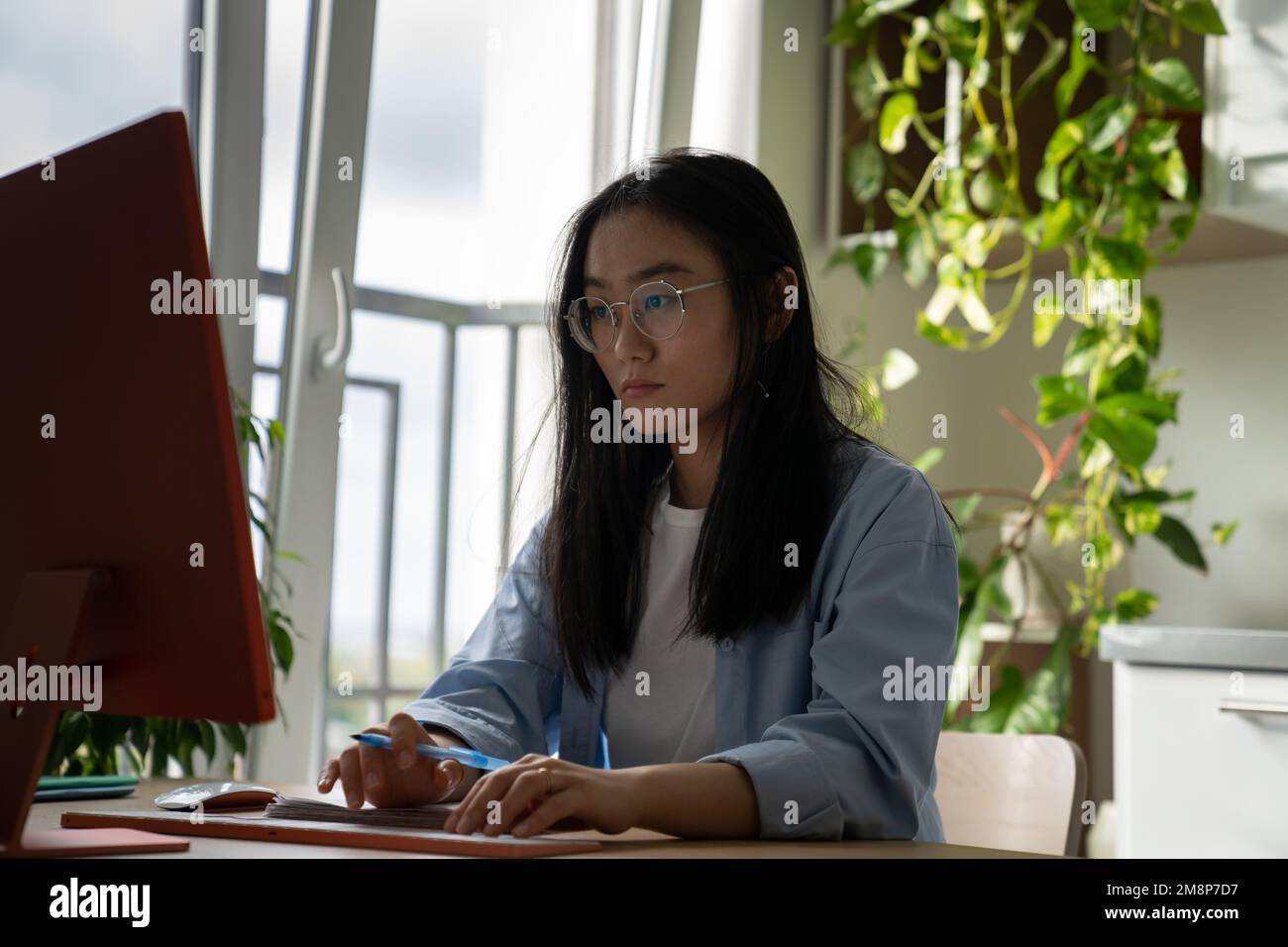 Focused Asian woman IT developer wearing glasses writing code on ...