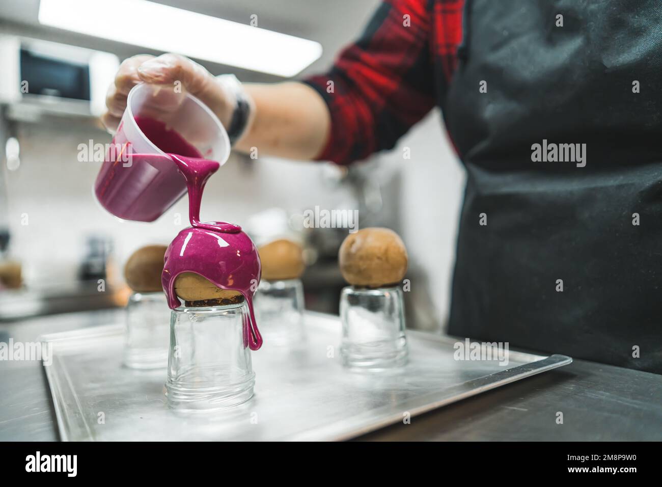 Professional female baker wearing black apron pouring pink glaze over ...