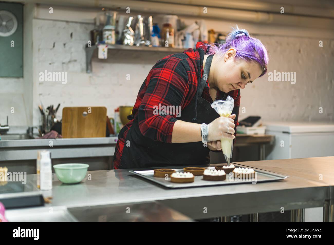 Female professional baker with purple hair piping buttercream frosting ...