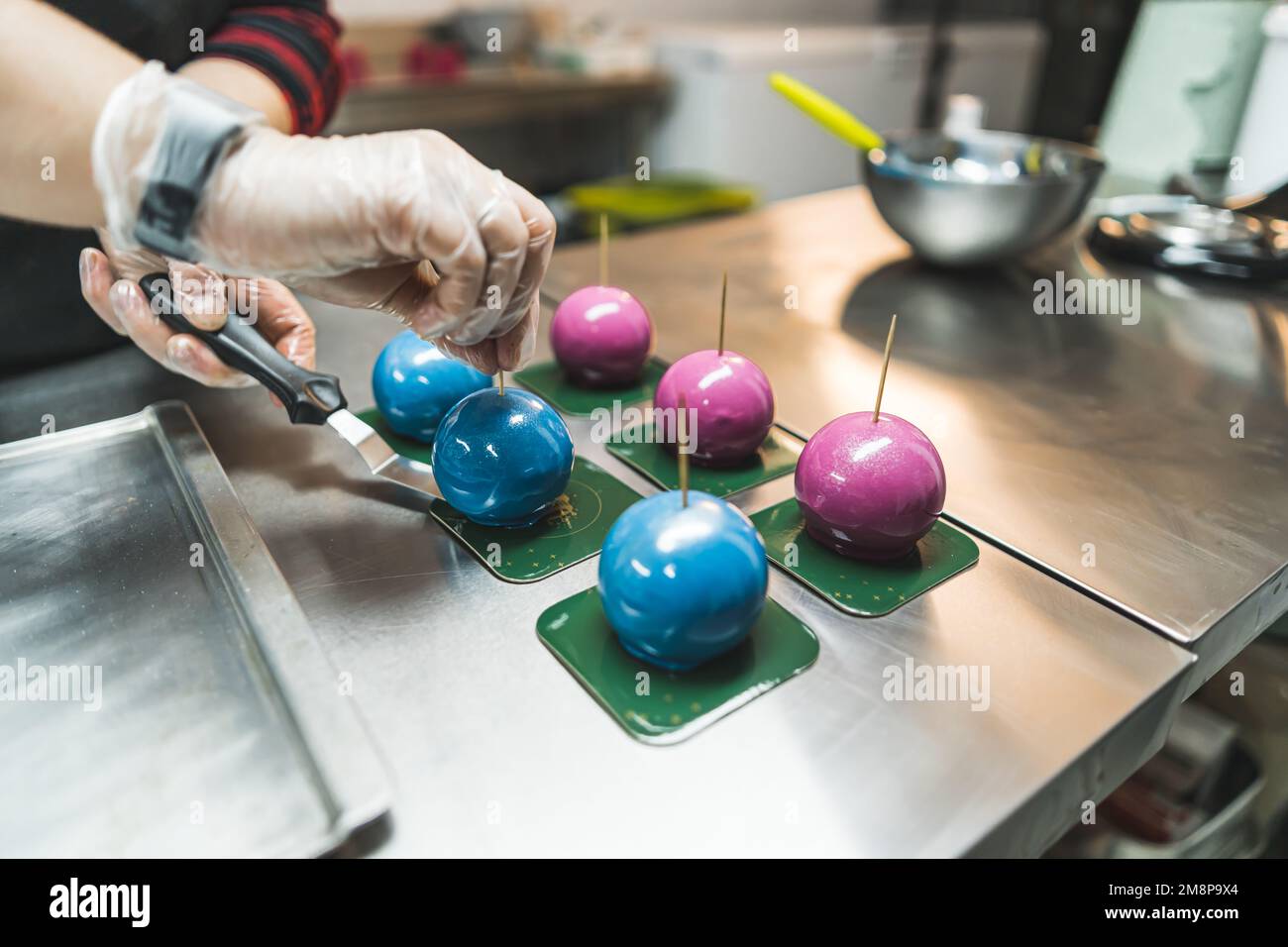 Unrecognisable baker placing spherical mousse desserts onto square ...