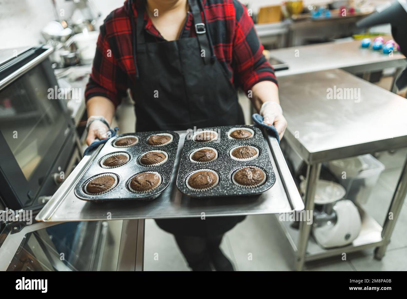 Female baker wearing black apron walking to the oven to bake tray of ...