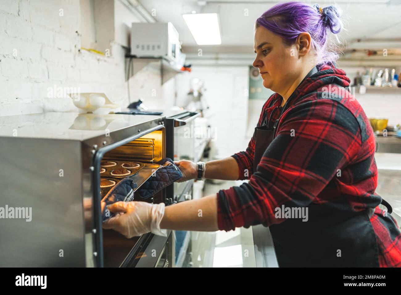 Female baked with purple hair wearing black apron putting tray of ...
