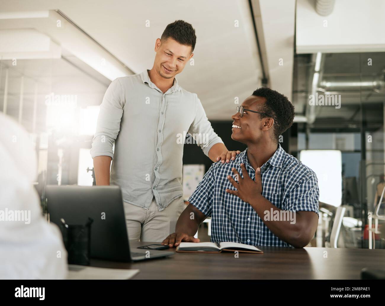 Two diverse businessmen talking at a desk discussing new project on laptop. Mentor complimenting ...