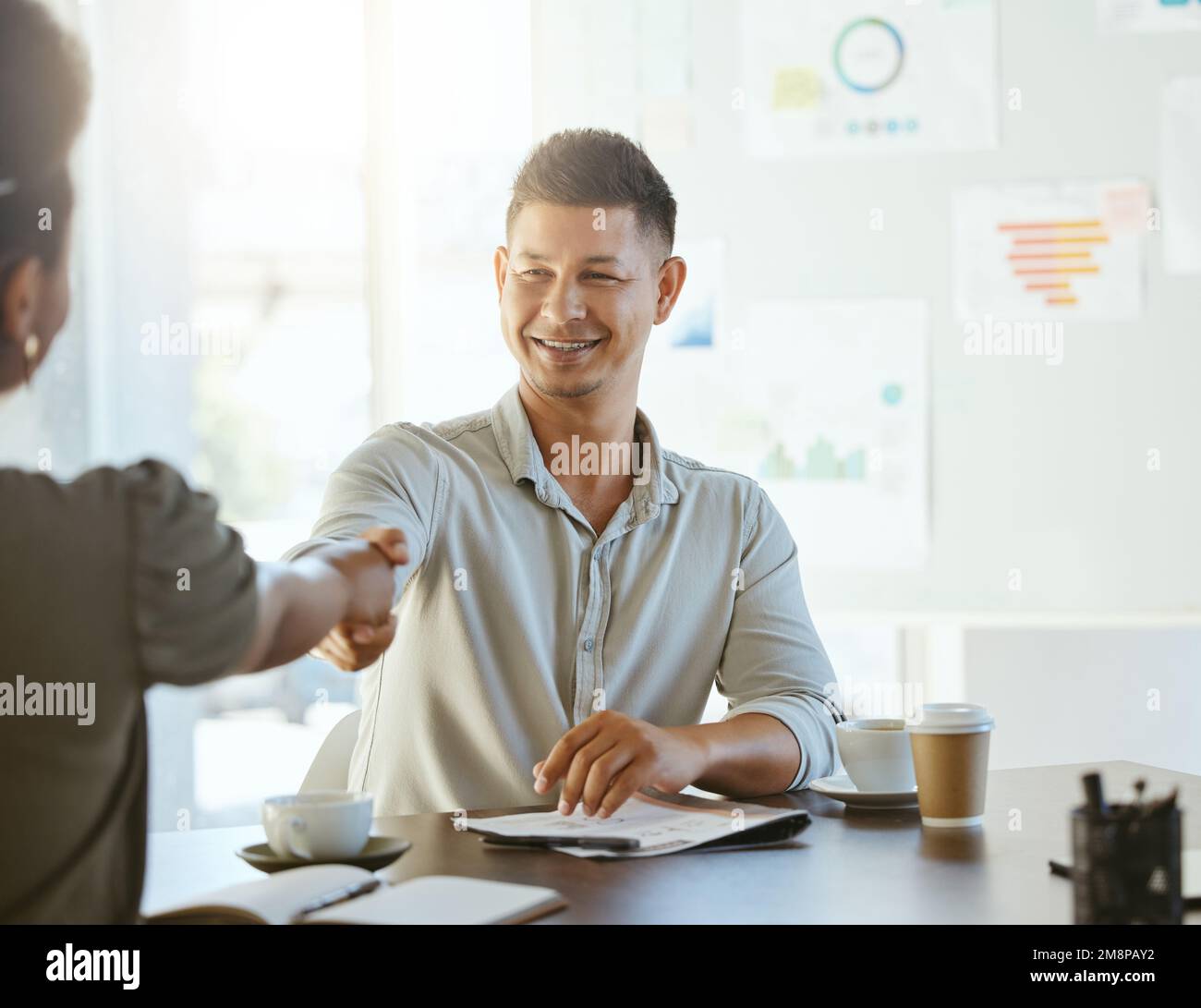Two businesspeople shaking hands while in an office together at work ...