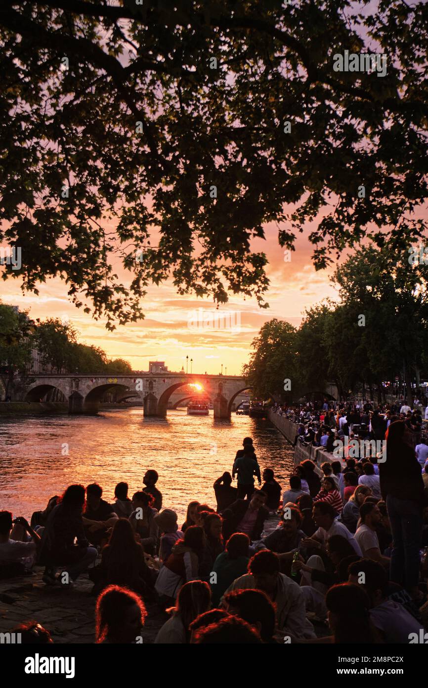 Paris, France - May, 2022: Crowd People have picnic on seine river bank at sunset in Le Marais ...