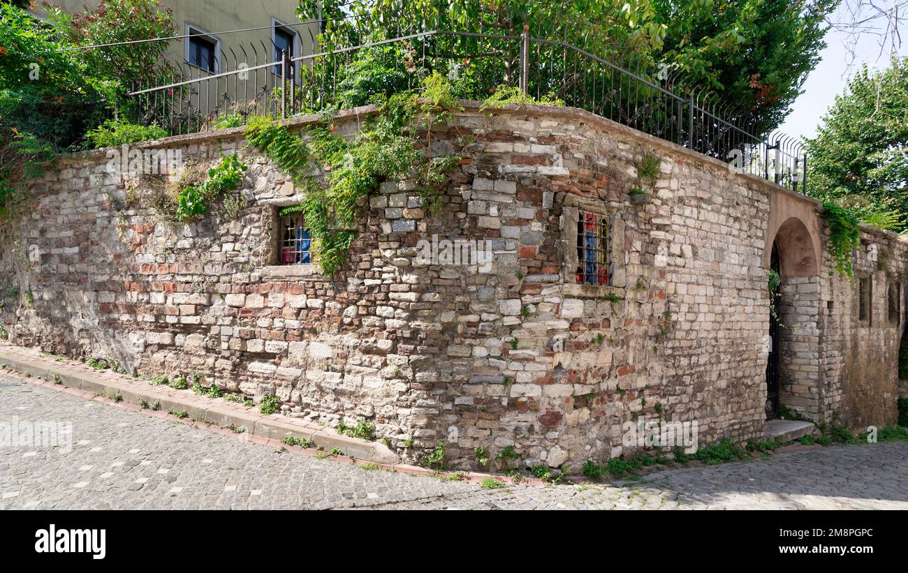 Old abandoned building, with weathered stone wall, and wrought iron windows, partially covered ...