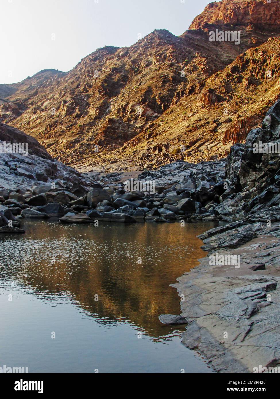 The cliffs of the Fish River Canyon, in the late golden afternoon light, reflecting in the calm ...