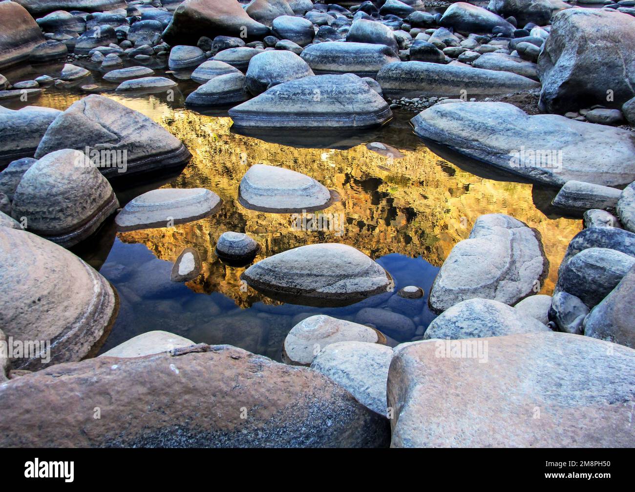 Golden colored cliff, reflecting in a pool between smooth rounded ...