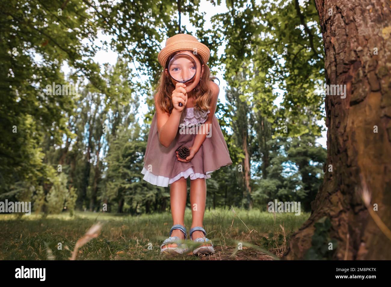 Cute little girl looks through a magnifying glass at the camera. Bottom ...