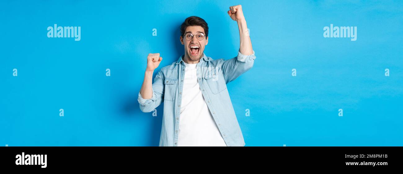 Excited handsome man triumphing, raising hands up and shouting for joy ...