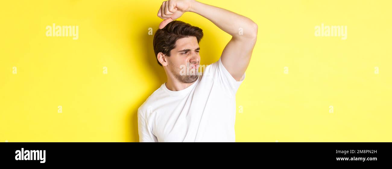 Man in sweat smelling his armpit, standing in white t-shirt and ...