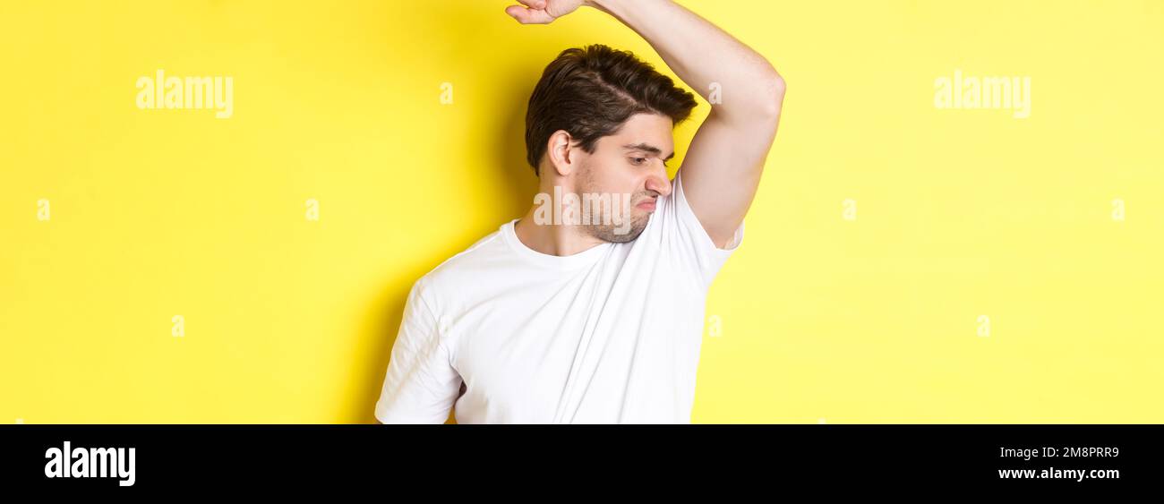 Man in sweat smelling his armpit, standing in white t-shirt and ...