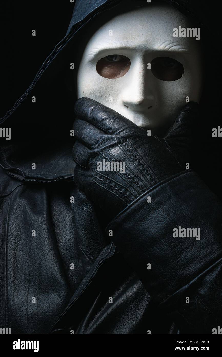 Man in terrible face mask staring at camera against dark background ...