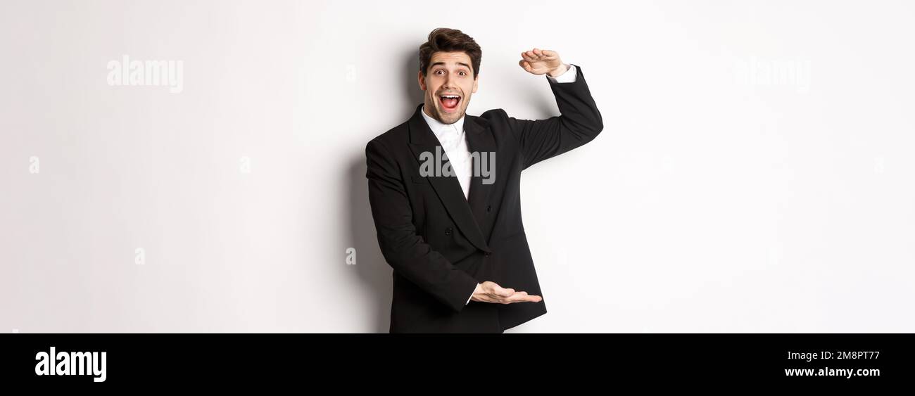 Portrait of excited handsome man in suit, shaping big object on copy ...