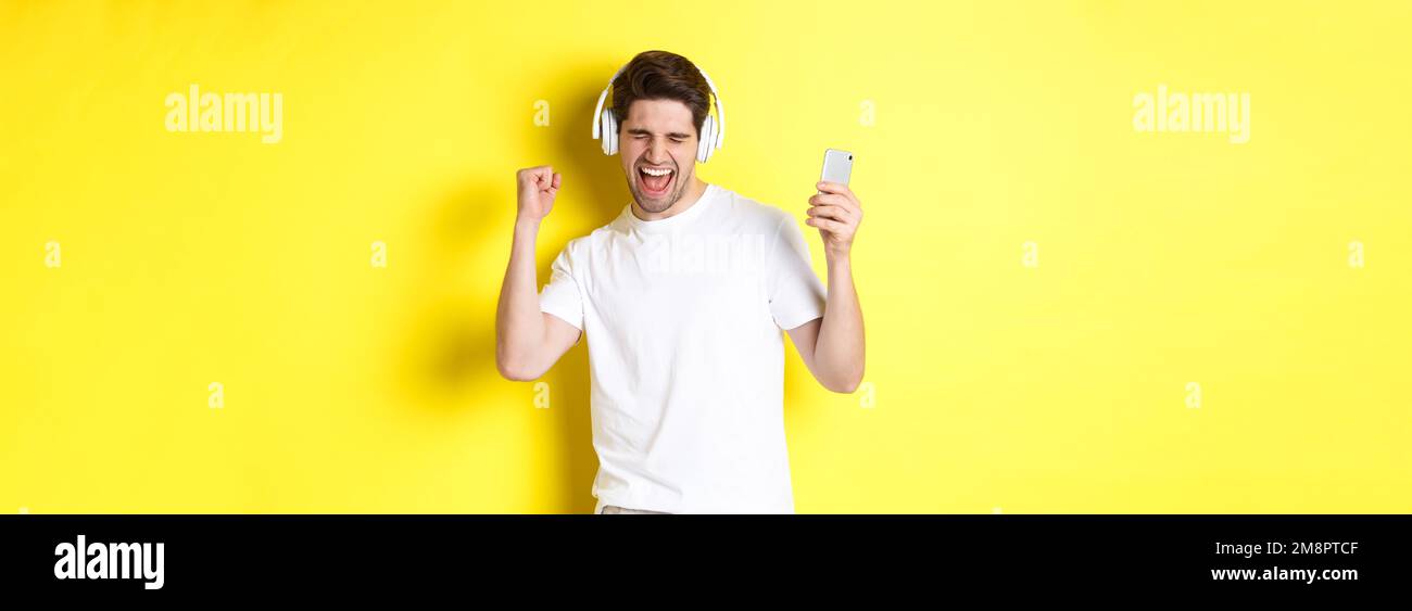 Happy man dancing and listening music in headphones, holding mobile ...