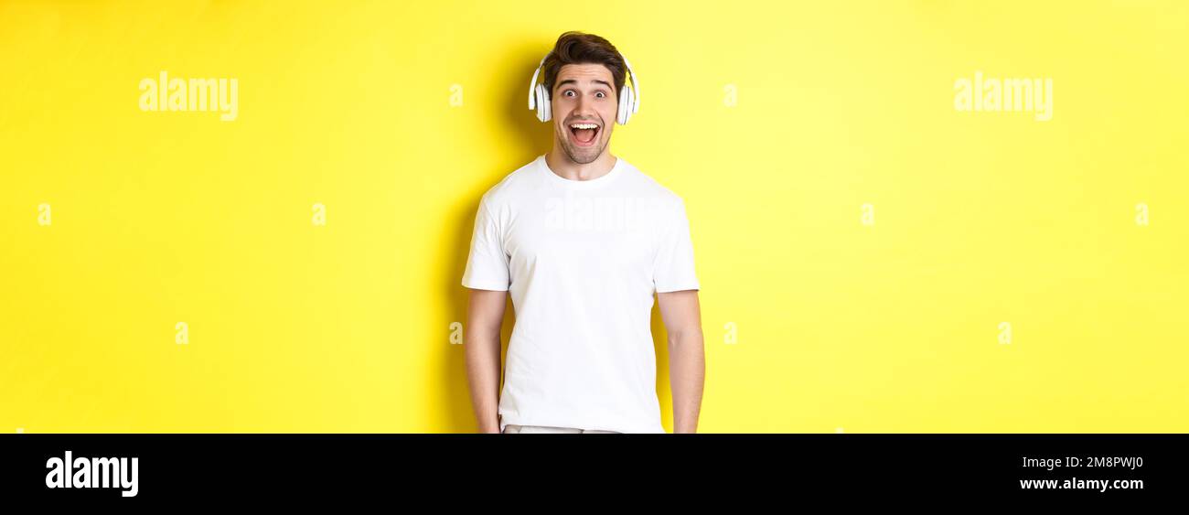 Man in headphones looking surprised, standing against yellow background ...