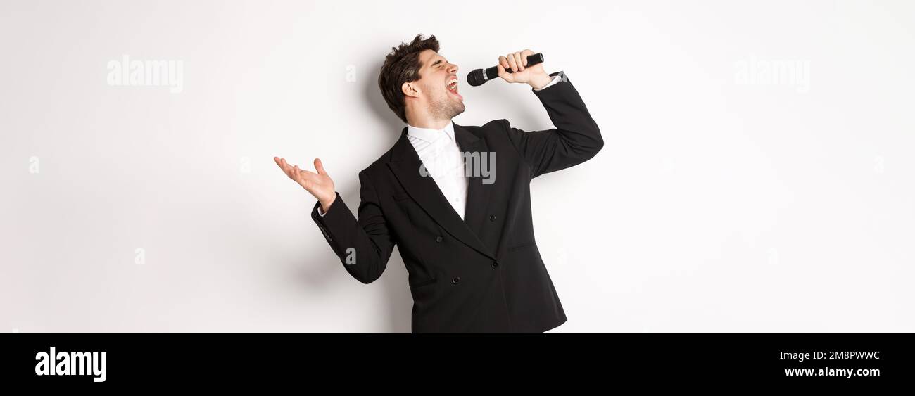 Portrait of handsome man singing a song with passion, standing in black ...