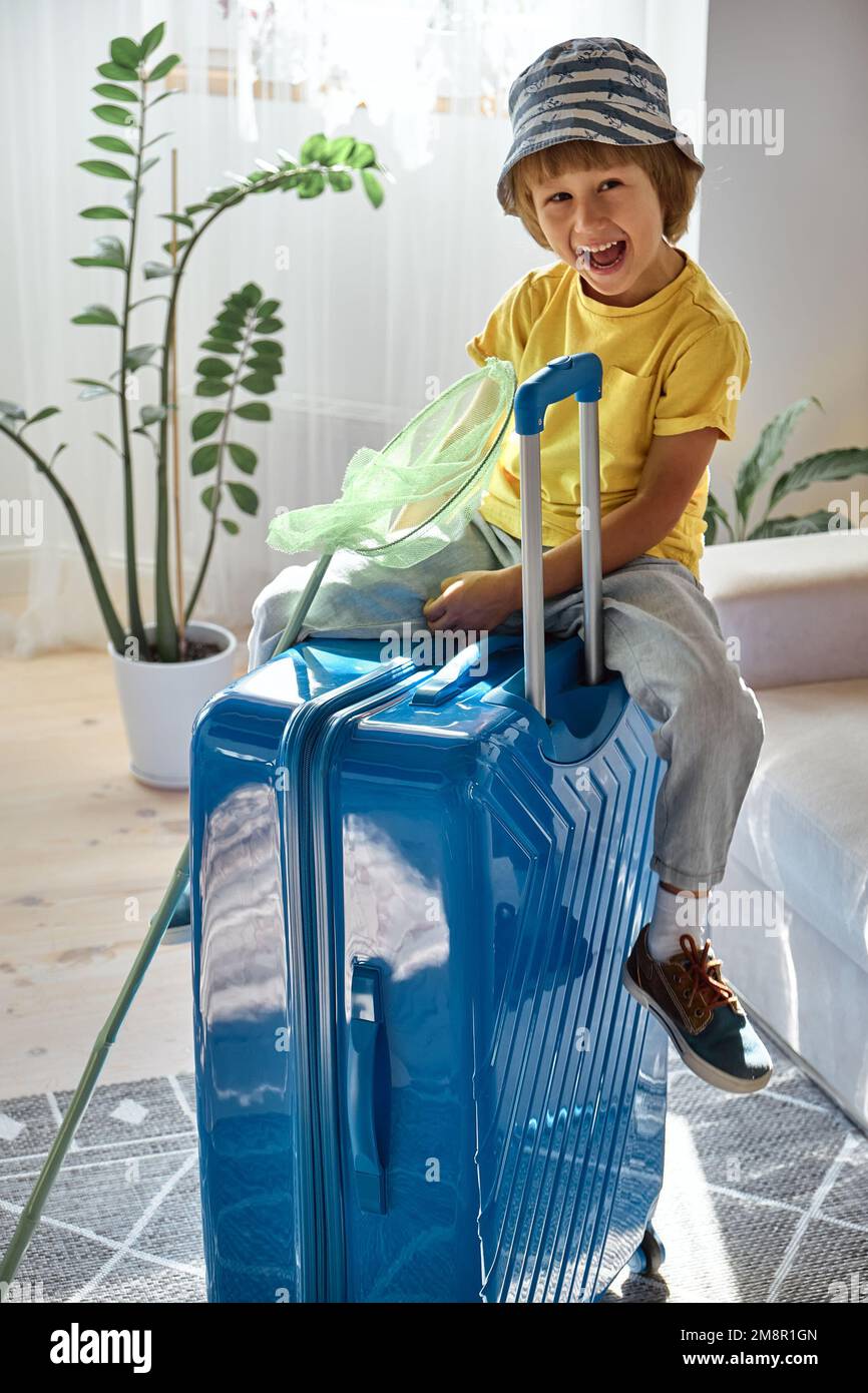 A child sitting on a suitcase have fun and laughs, waiting for a trip ...