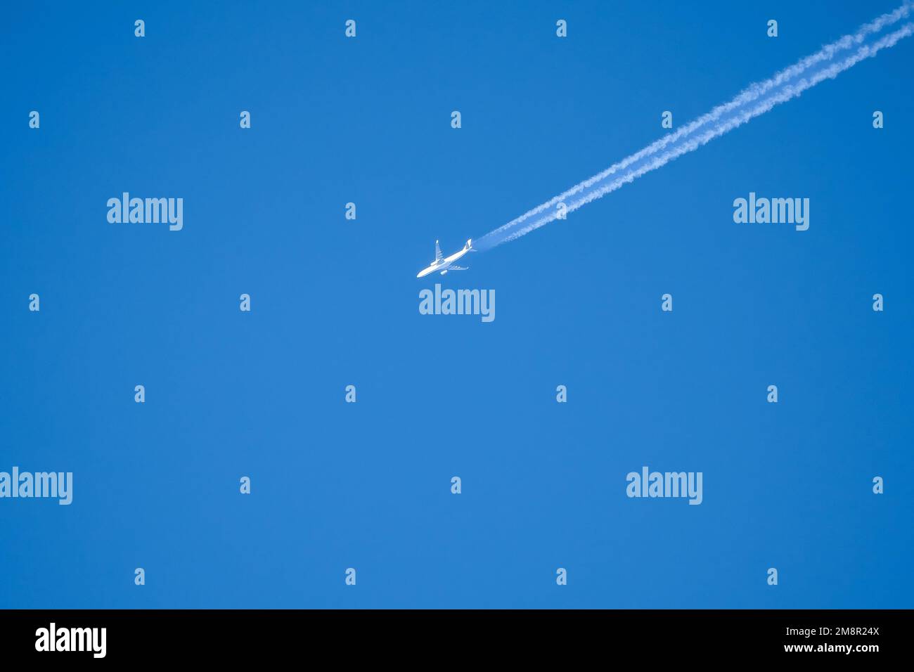 twin engine jet airliner in deep blue sky with vapour contrails ...