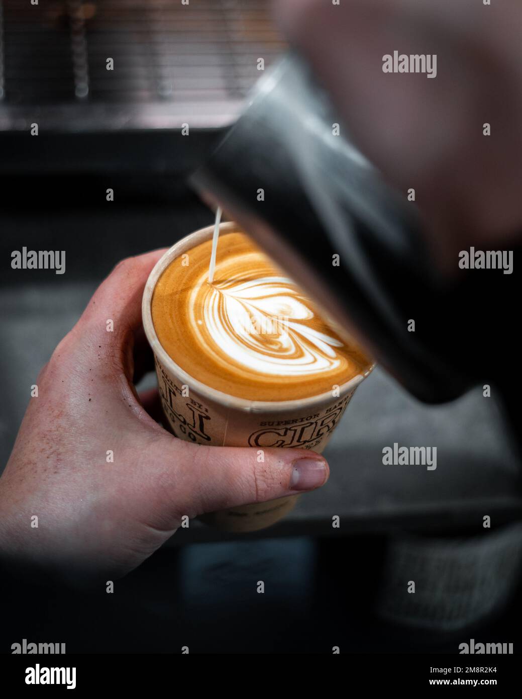 A vertical shot of a man making a drawing on a cappuccino in his hand ...