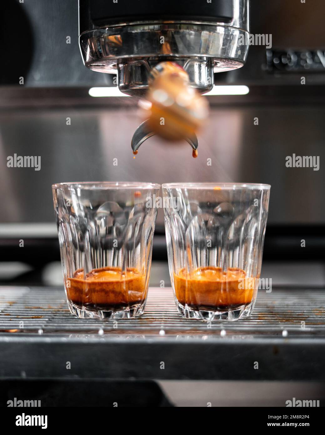 A vertical shot of coffee dripping from the machine into glass cups ...