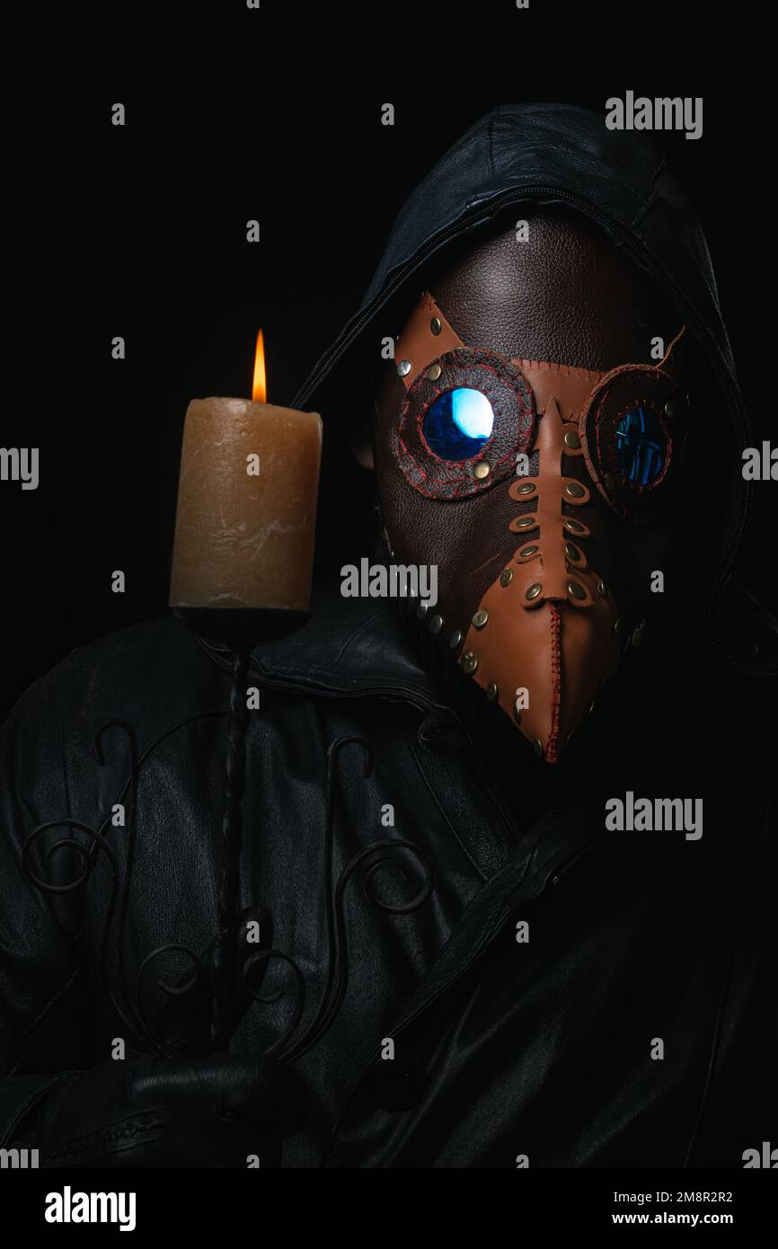 Plague doctor with crow-like mask and candle isolated on black ...