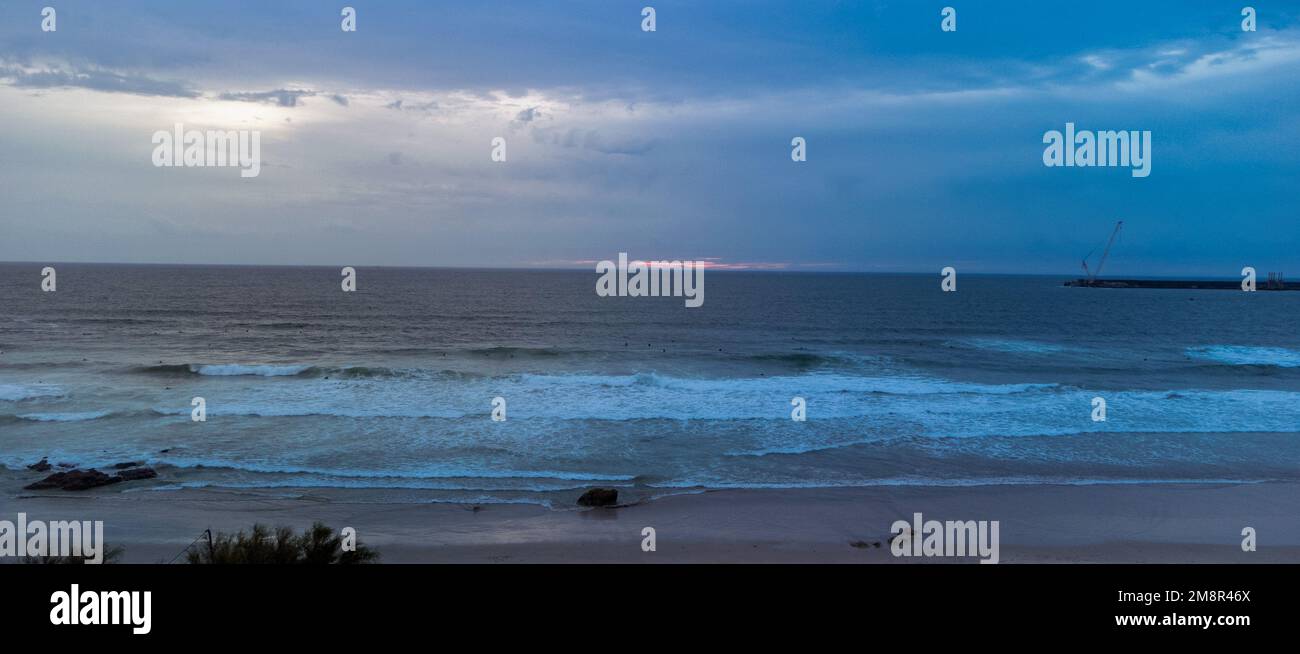 A panoramic shot of a wavy sea and people surfing near the beach at ...