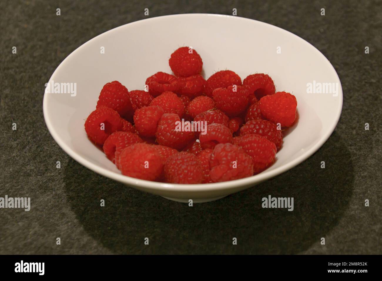 raspberries in a white bowl on a table Stock Photo - Alamy
