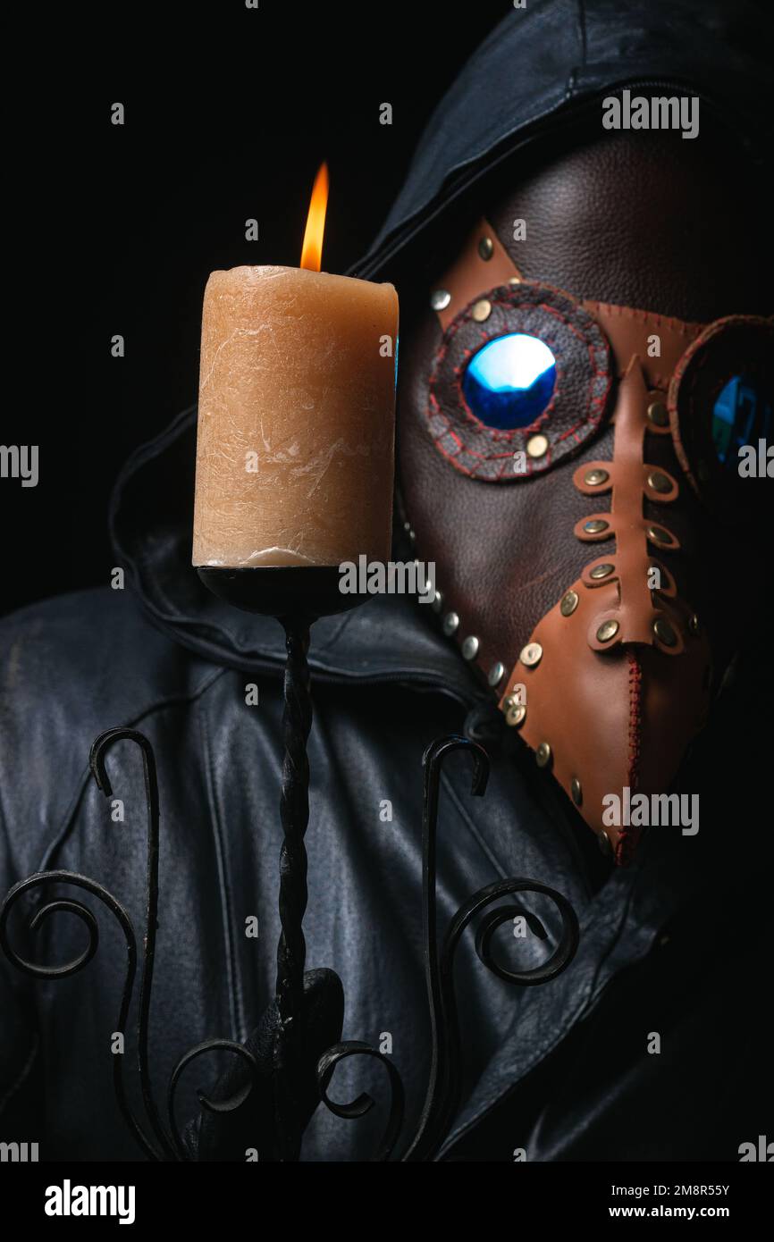 Plague doctor with crow-like mask and candle isolated on black ...
