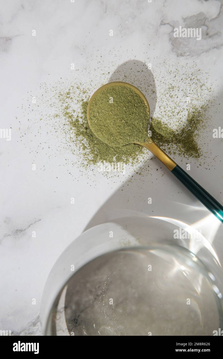 Green powder in spoon and glass of water. Concept of nutritional ...